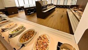 Uma área de buffet com diversos pratos, um espaço de refeições com cadeiras e um balcão com uma máquina de café.