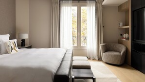 Quarto de hotel com uma cama grande, um sofá pequeno, uma cadeira, uma televis ão e uma janela com cortinas.