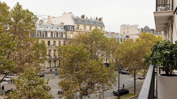 Vista de uma rua da cidade com edifícios históricos, árvores e carros estacionados.