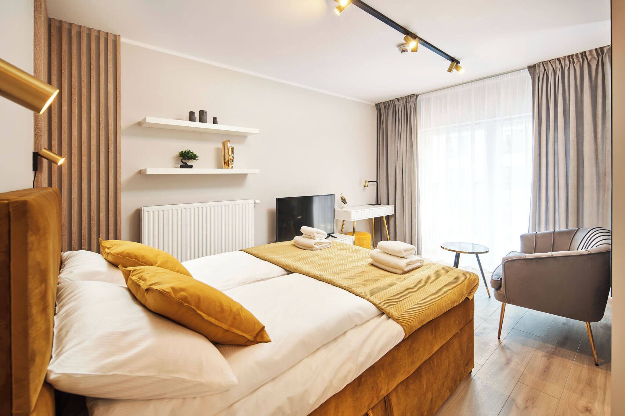 Quarto de hotel moderno com uma cama grande, uma escrivaninha com computador, uma cadeira e uma janela com cortinas.