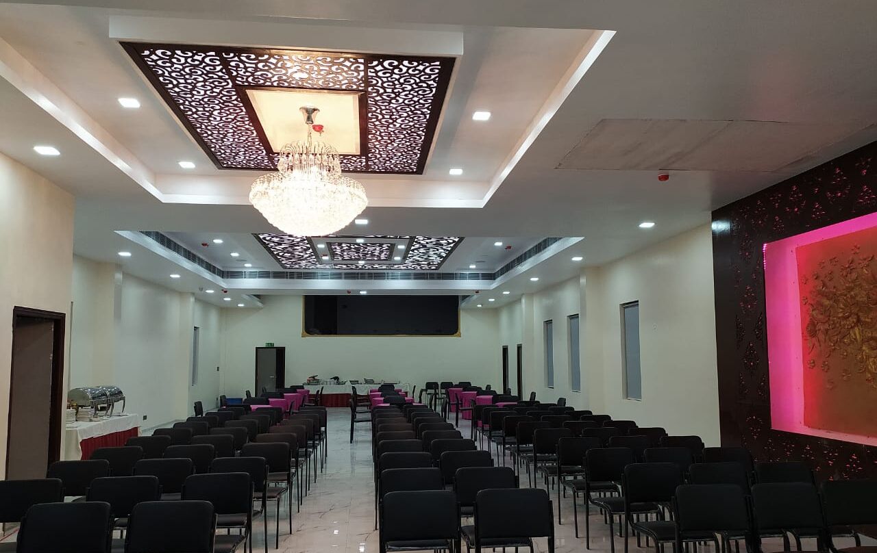 Uma sala de conferências com fileiras de cadeiras, uma tela grande e um candelabro.