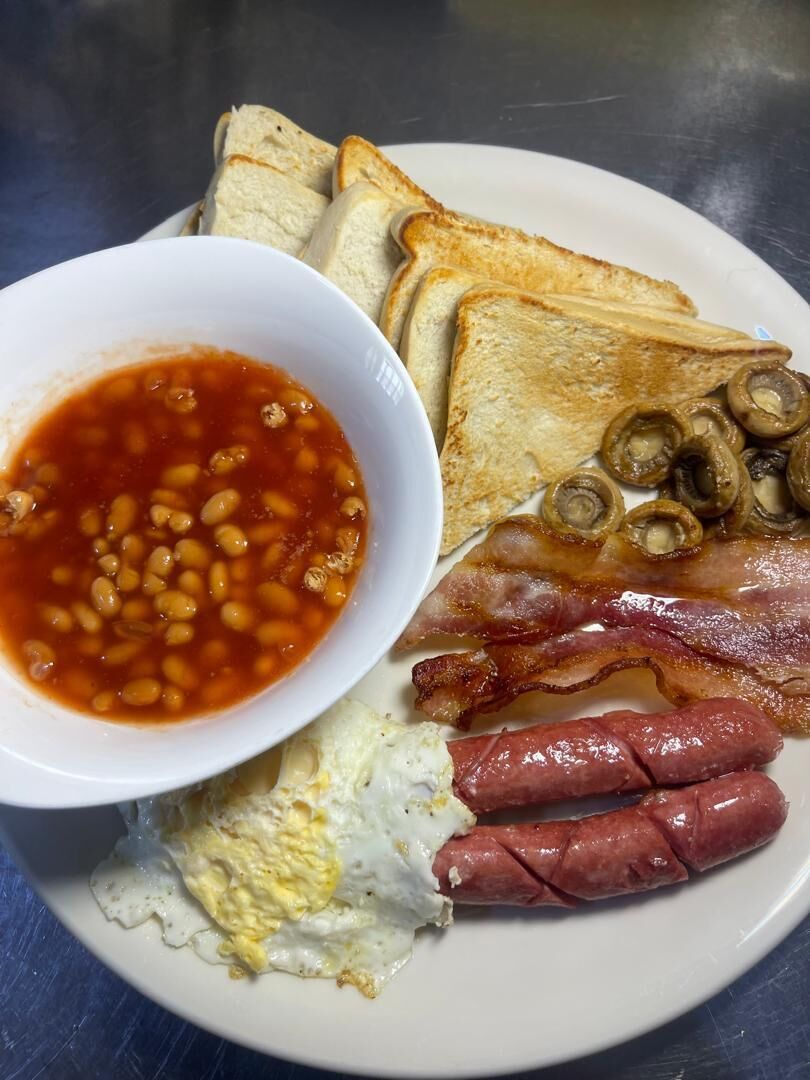 Um prato de comida de café da manhã com torradas, feijão, cogumelos, bacon, linguiça e ovos.