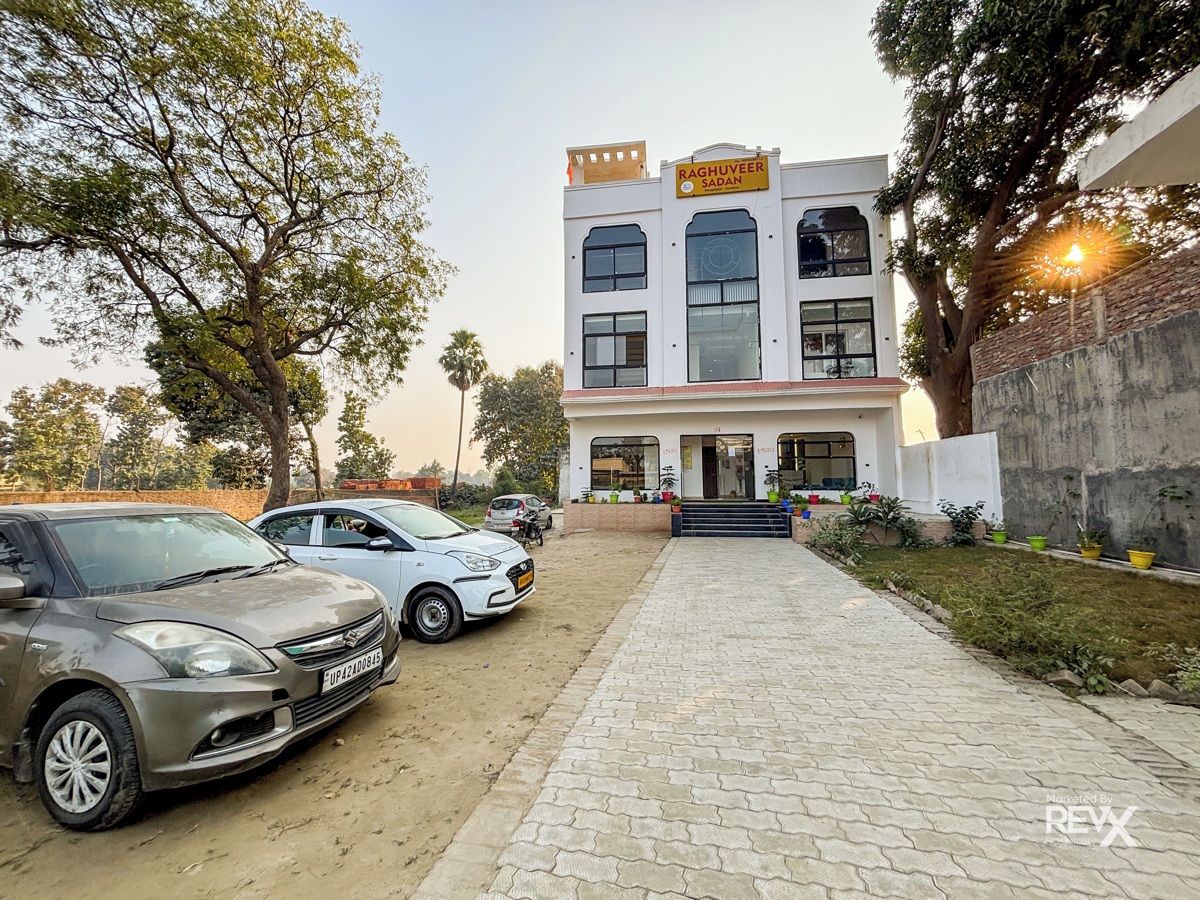 Um edifício com uma placa indicando "RAGHUYEER SUDAN" e um caminho de paralelepípedos que leva à entrada.