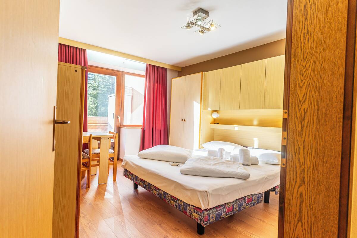 Quarto de hotel com cama, guarda-roupa de madeira e um espaço de refeições com cadeiras e mesa.