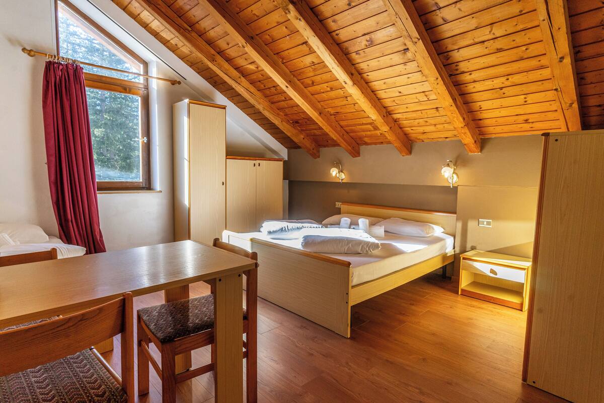 Quarto com teto de madeira, uma cama, escrivaninha e uma cadeira.