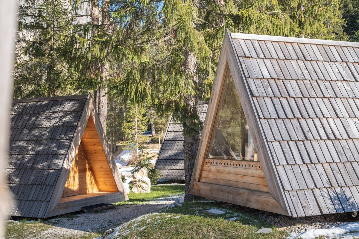 Duas cabanas de madeira em formato de A numa área arborizada.