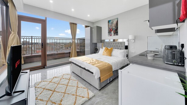 Quarto de hotel moderno com uma cama grande, televisão, área de cozinha e varanda com vista.