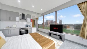 Quarto de hotel moderno com uma cama grande, cozinha compacta, televisão e varanda com vista para a cidade.