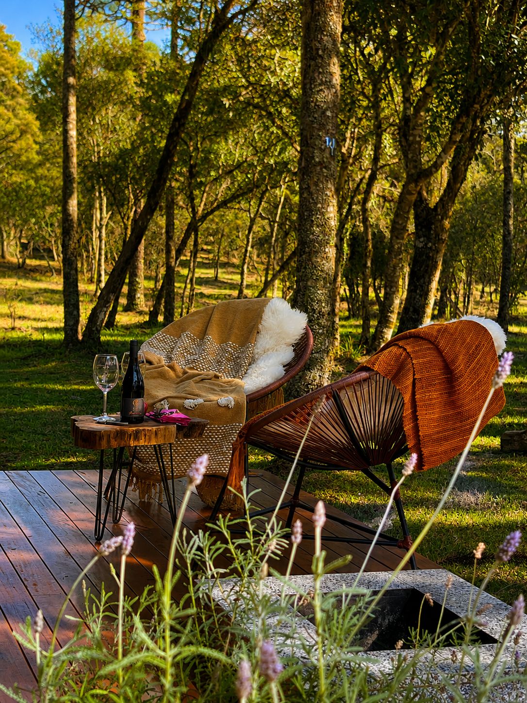 Uma área de estar ao ar livre com uma cadeira de vime e uma mesa, cercada por árvores e grama.
