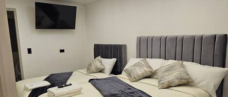 Quarto moderno com cama grande, TV fixada na parede e iluminação embutida no teto.