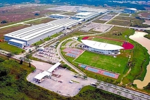 Um complexo industrial com edifícios grandes, uma estrutura circular e uma área de estacionamento.