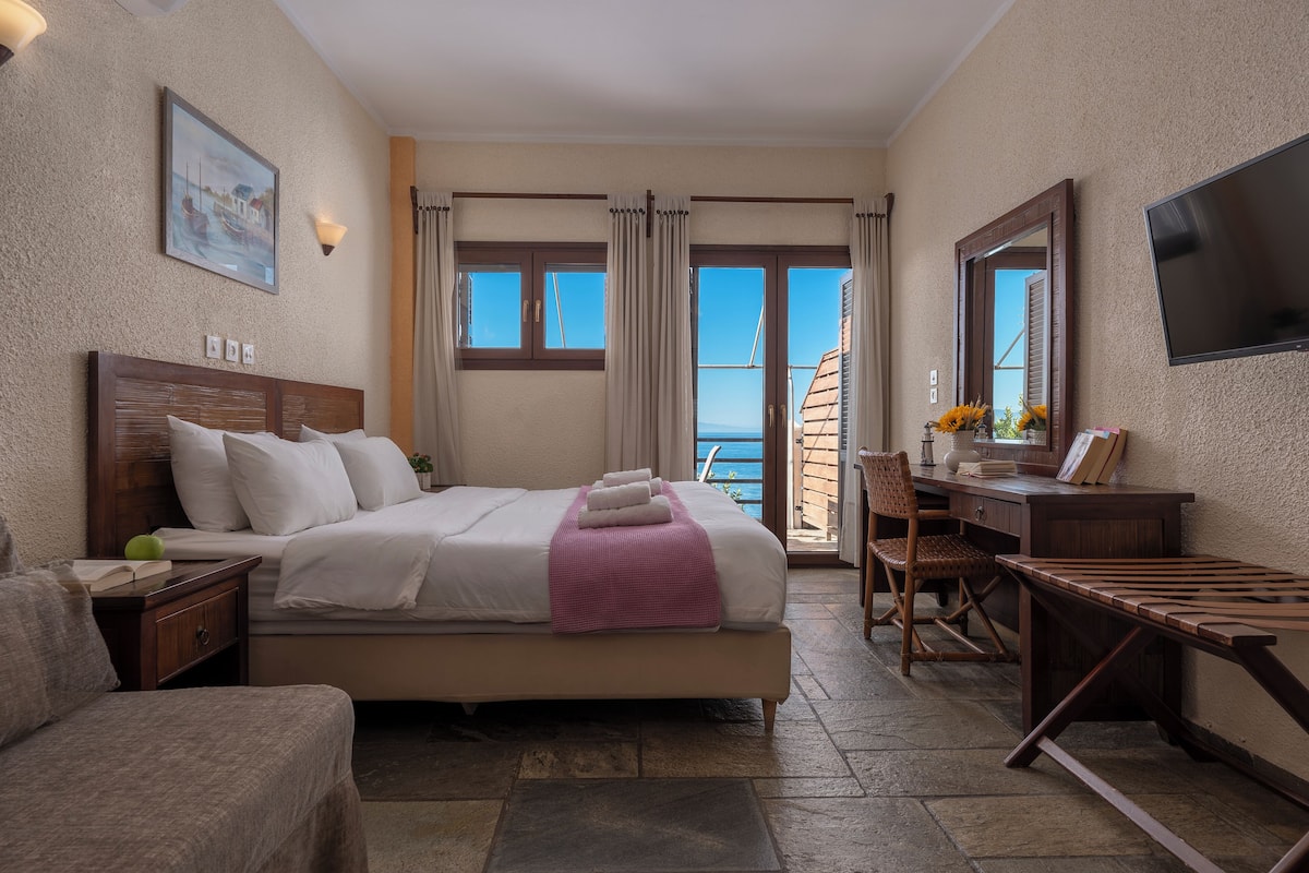 Quarto de hotel com cama, escrivaninha, cadeira, televisão e vista para o mar.