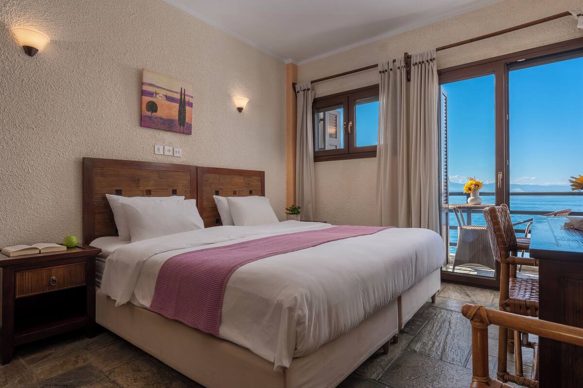 Quarto de hotel com uma cama grande, mesa de cabeceira, uma cadeira e vista para o mar.