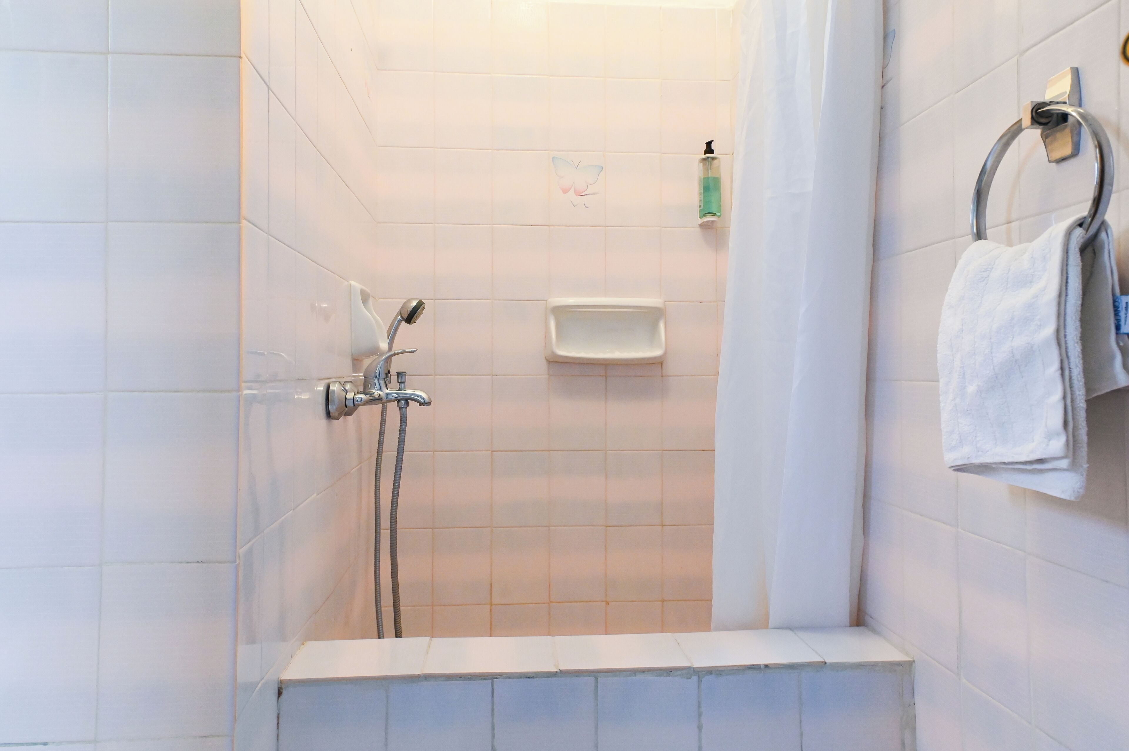 Um pequeno espaço de chuveiro revestido com azulejos, com chuveiro manual, dispensador de sabonete e porta-toalhas.