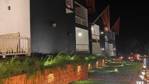 Vista noturna de um edifício com piscina, um caminho de tijolos e uma pequena área de jardim com plantas.