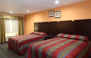 Quarto de hotel com duas camas, uma janela grande com cortinas e uma televisão presa à parede.