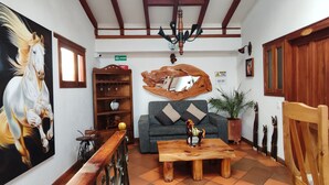 Um quarto com uma mesa de centro de madeira, um sofá cinza com almofadas pretas, uma estante de madeira, uma grande pintura de um cavalo, uma cadeira de madeira e uma planta em vaso.