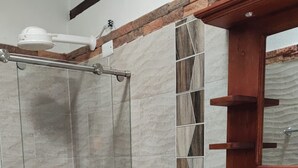 Uma casa de banho moderna com cabine de duche em vidro, sanita, lavatório e uma prateleira de madeira sobre o espelho.