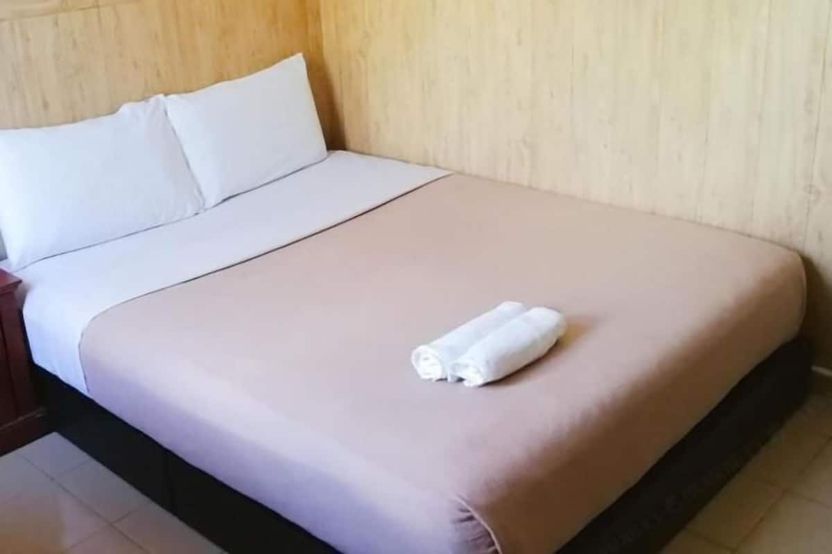 Cama bem arrumada com edredom branco e bege, toalha branca enrolada na cama e cabeceira de madeira.