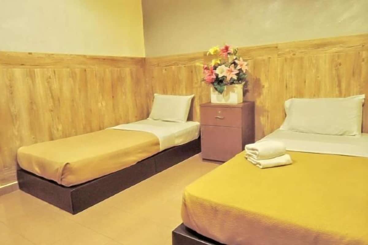 Quarto de hotel com duas camas, painéis de madeira nas paredes, mesa de cabeceira com um vaso de flores e uma gaveta pequena.