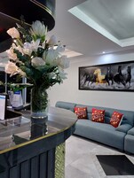 Uma área de recepção com uma mesa de vidro, um vaso de flores, um sofá azul com almofadas vermelhas e uma pintura de um cavalo na parede.