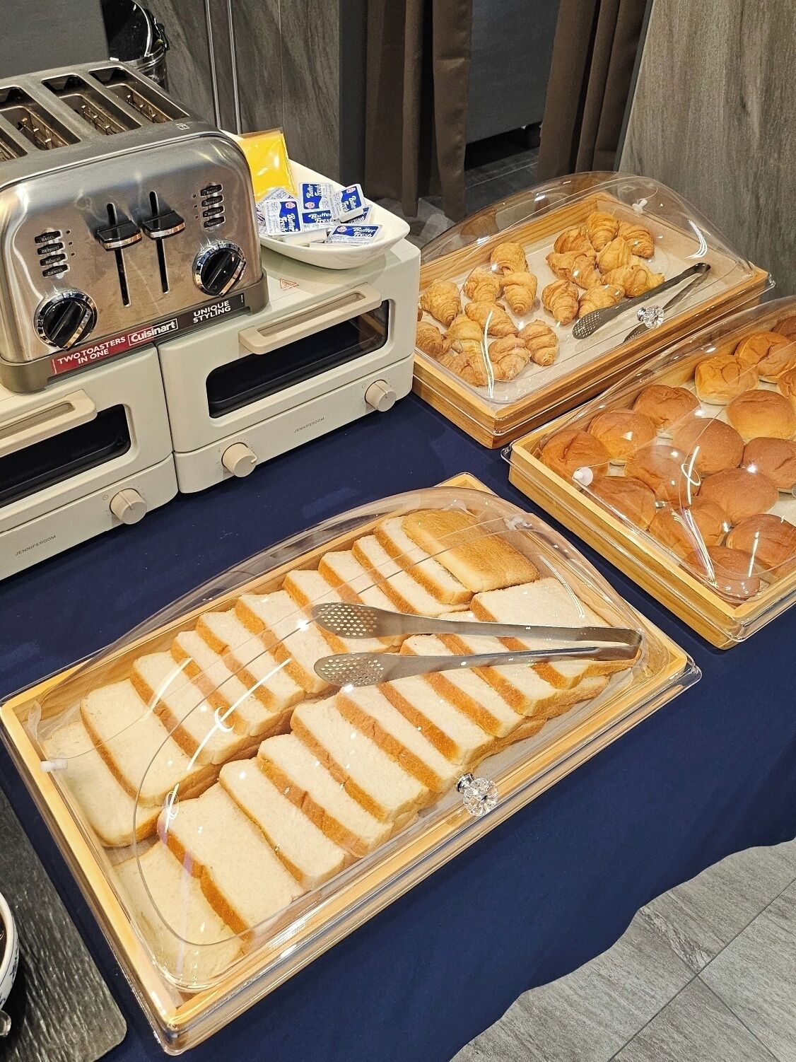 Uma mesa de buffet com diversos alimentos, incluindo pão, doces e uma torradeira.