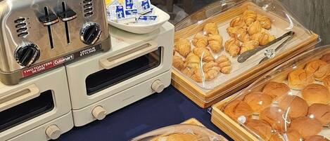 Uma mesa de buffet com diversos alimentos, incluindo pão, doces e uma torradeira.
