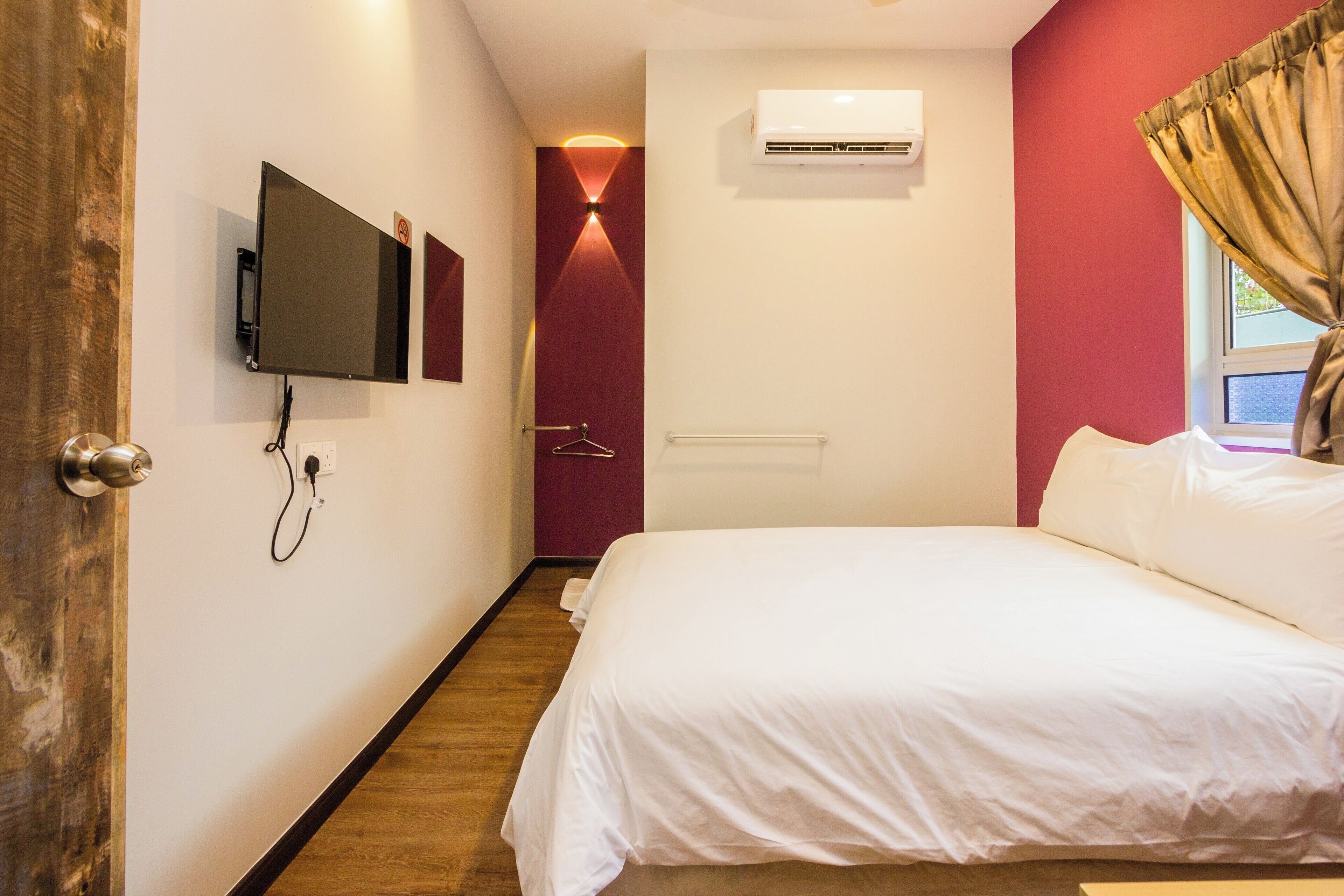 Quarto de hotel com cama, televisão na parede, aparelho de ar condicionado e janela com cortinas.