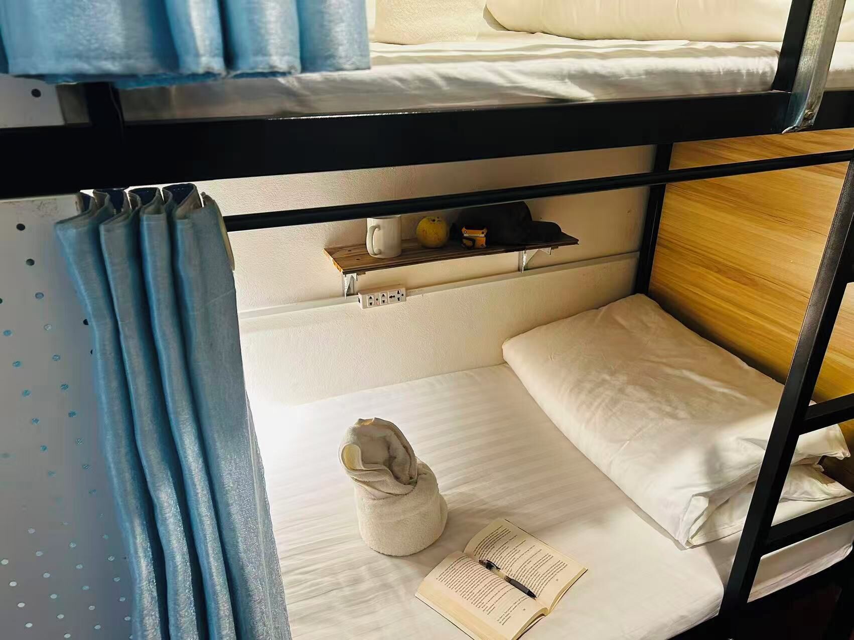 Quarto com beliche, uma prateleira sobre a cama inferior, uma toalha e um livro aberto na cama de baixo.