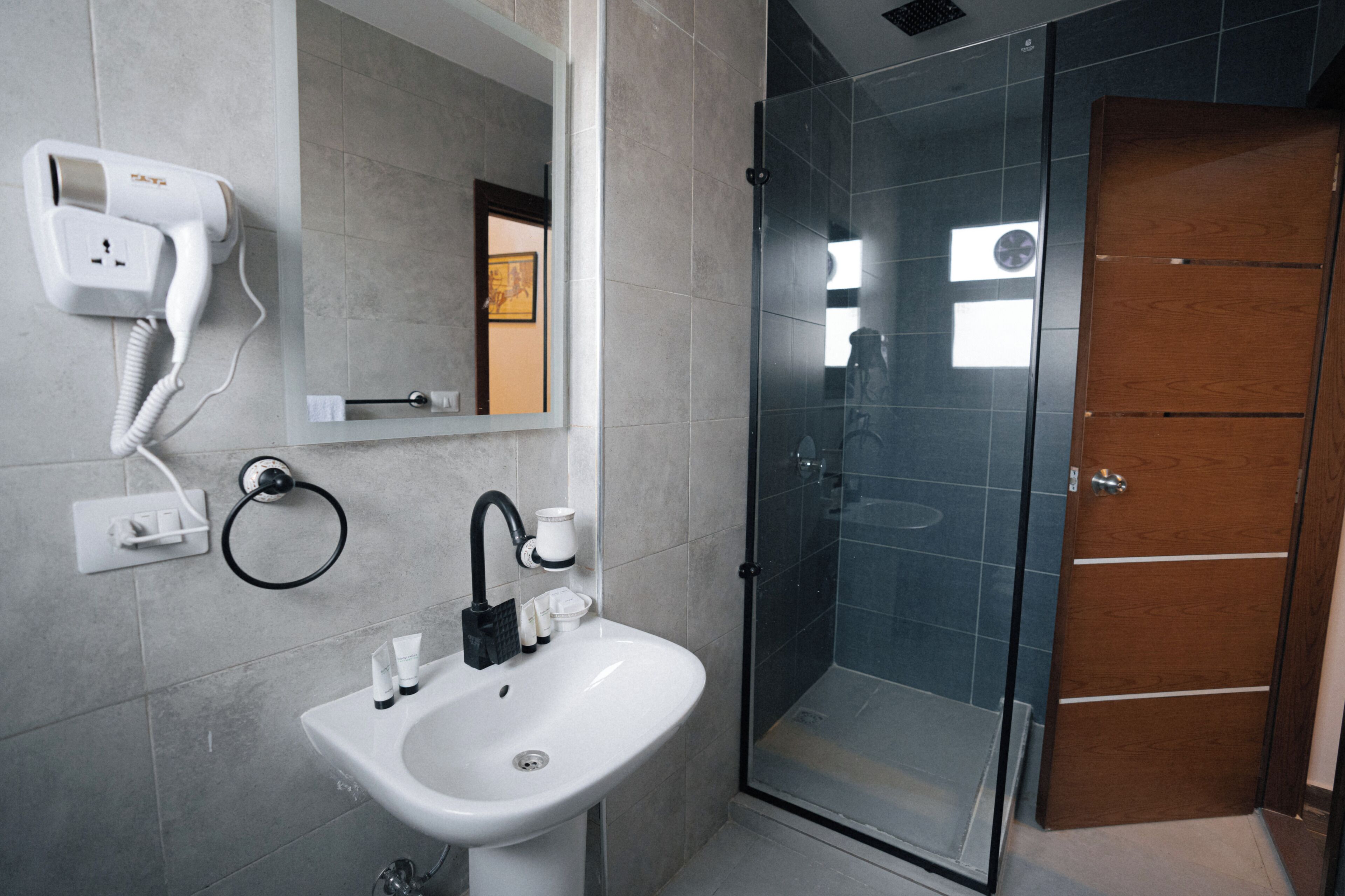 Casa de banho com lavatório branco, secador de cabelo e cabine de duche em vidro.