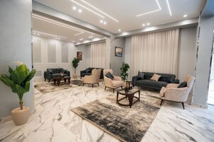 Uma sala de estar moderna com piso de mármore, um sofá grande, poltronas, uma mesa de centro e um vaso com planta.