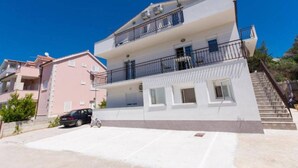 Um edifício residencial de vários andares com varandas, um carro estacionado em frente e uma escadaria que leva à entrada.