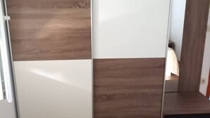 Quarto com parede de painel de madeira e uma seção branca. Há uma cama com colcha branca e cabeceira de madeira.