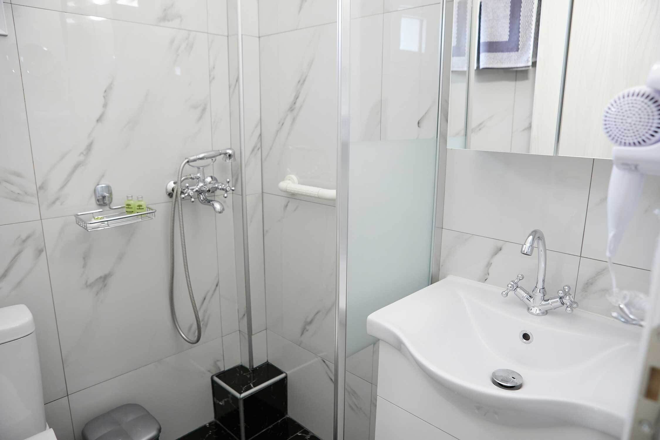 Casa de banho com chuveiro envidraçado, lavatório branco com torneira moderna e secador de cabelo sobre a bancada.