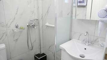 Casa de banho com chuveiro envidraçado, lavatório branco com torneira moderna e secador de cabelo sobre a bancada.