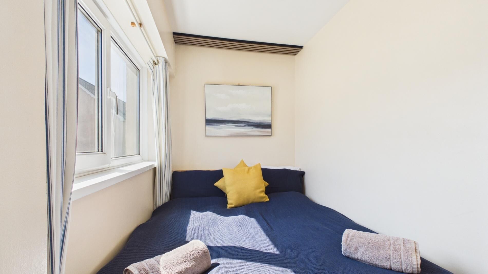 Quarto com cama, janela, quadro e toalhas.
