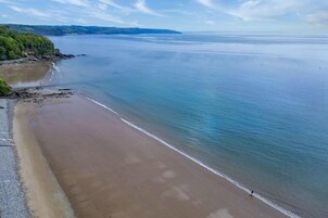 Uma praia costeira com areal, mar calmo e colinas ao longe.