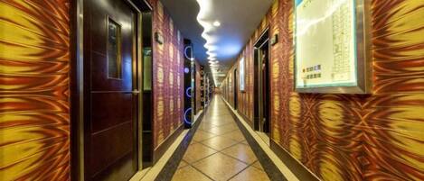 Corredor de hotel com paredes estampadas, portas e piso ladrilhado.
