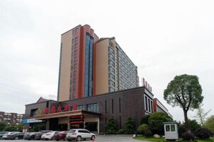 Hotel com vários andares, entrada destacada, estacionamento e uma pequena construção adjacente.