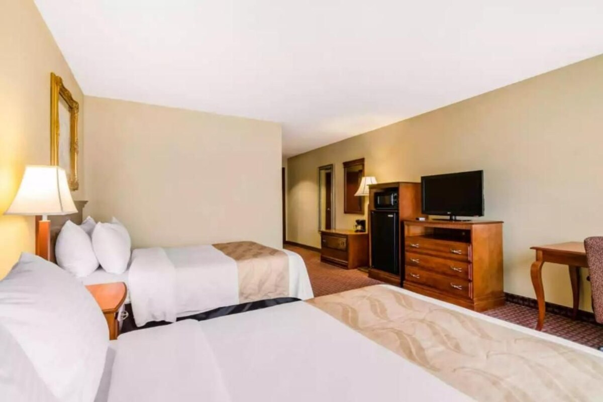 Quarto de hotel com duas camas, uma escrivaninha, uma televisão e uma cômoda.
