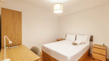 Quarto com cama de madeira, escrivaninha com abajur, mesa de cabeceira e luminária pendente.