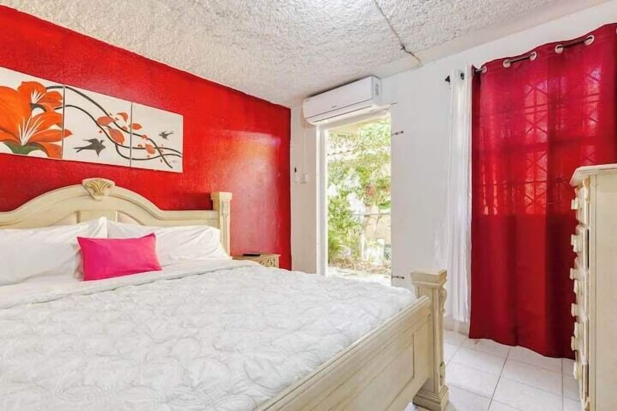 Quarto com cama branca, cortinas vermelhas e um quadro na parede.