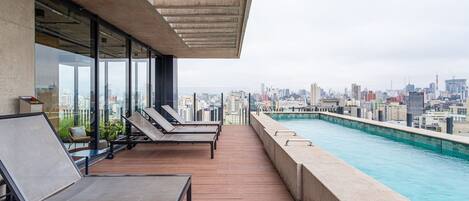 Uma área de piscina no terraço com espreguiçadeiras, vista para o horizonte da cidade e uma piscina com água cristalina.