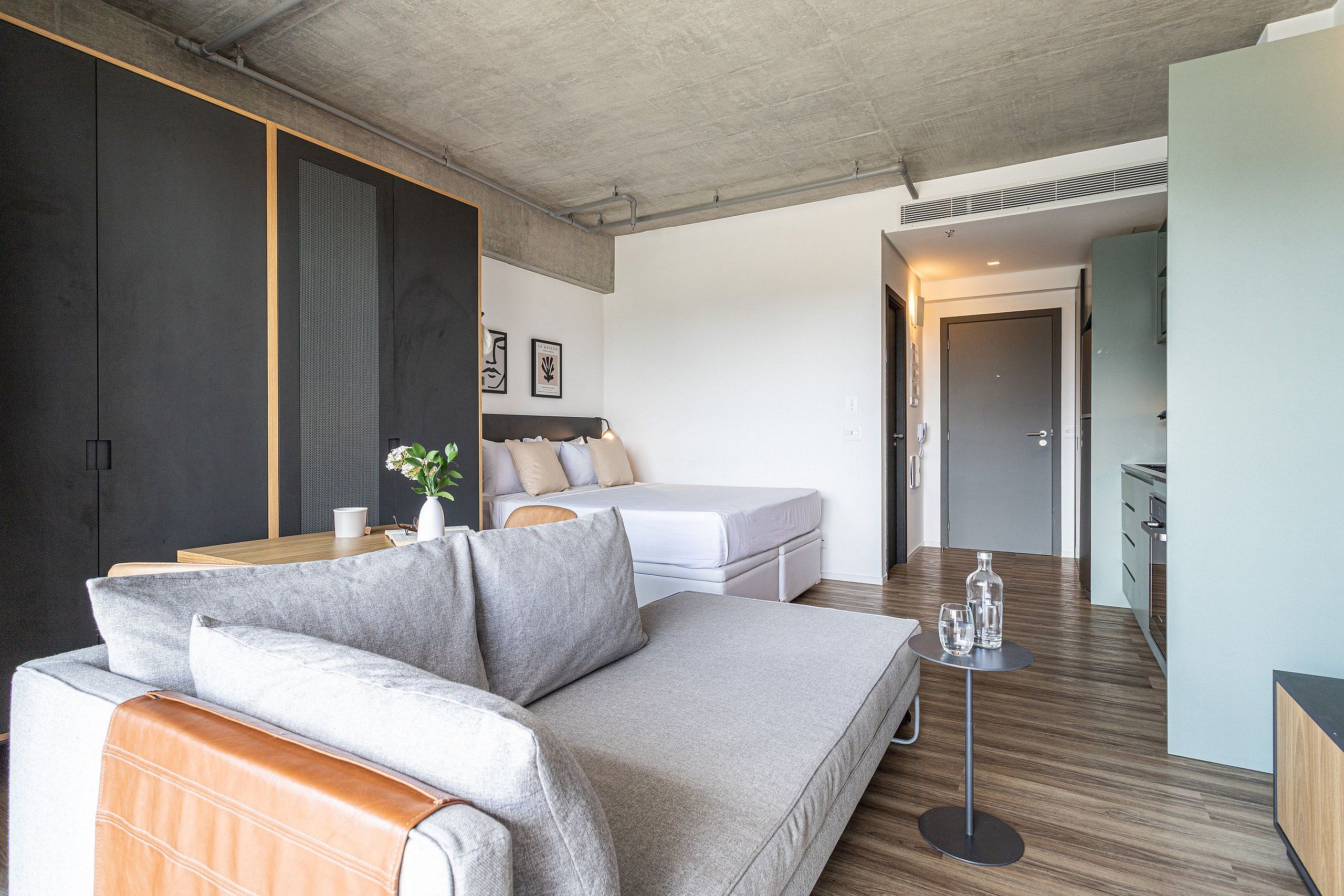 Um espaço de estar moderno com sofá, cama, pequena mesa e área de cozinha compacta.