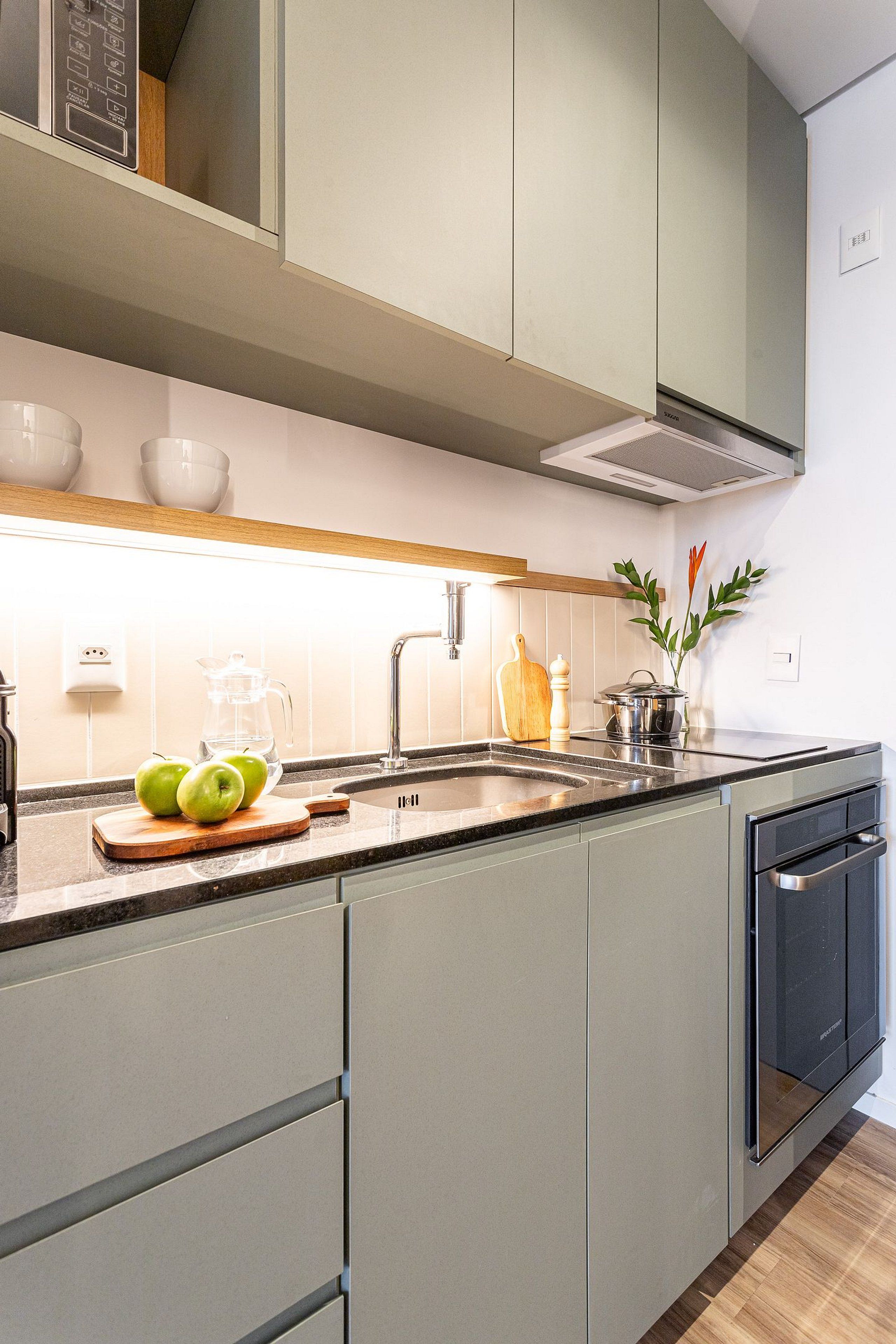 Uma cozinha moderna com forno embutido, pia e bancada com maçãs e tábua de corte.
