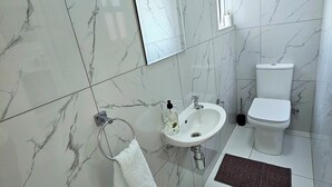 Um banheiro com piso de mármore branco, pia branca, vaso sanitário e espelho.