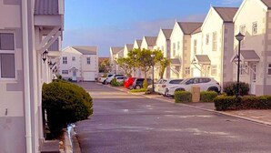 Rua residencial com casas, carros estacionados e céu claro.