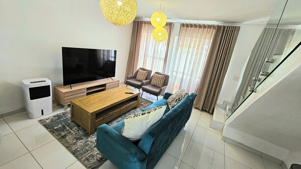 Uma sala de estar moderna com televisão de tela plana, mesa de centro de madeira, sofá azul e escada de vidro.