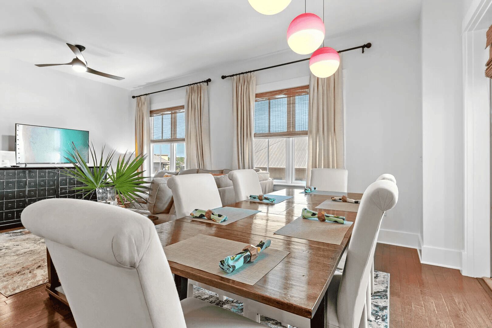 Uma sala de jantar moderna com uma mesa de madeira, cadeiras brancas e um ventilador de teto.