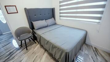 Um quarto com uma cama, uma cadeira e uma janela com persianas.